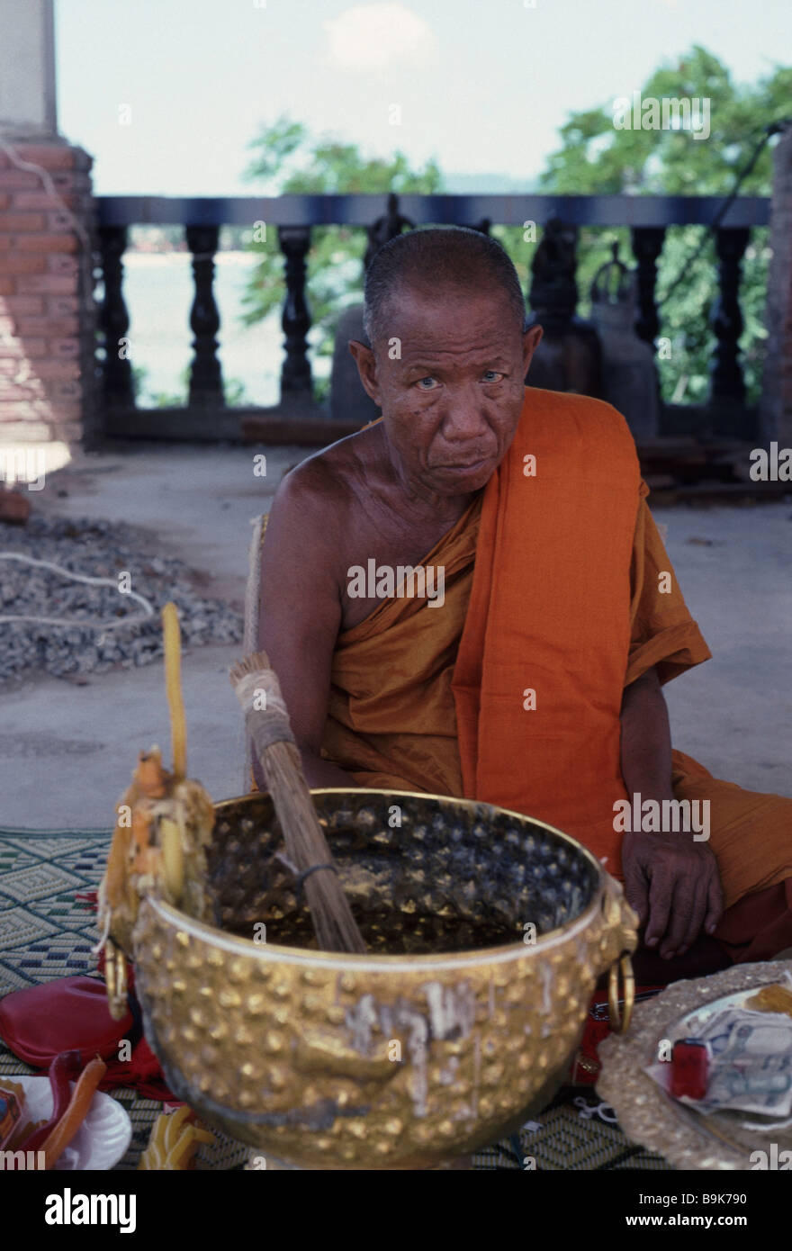 An serious elderly Buddhist monk sits near the entrance to big buddha ...