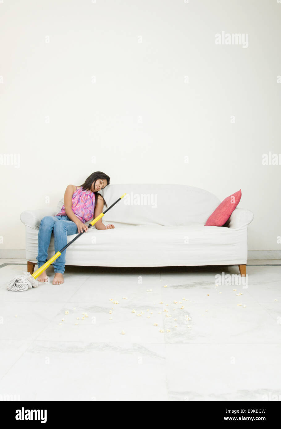 Woman holding a mop and resting on a couch Stock Photo - Alamy