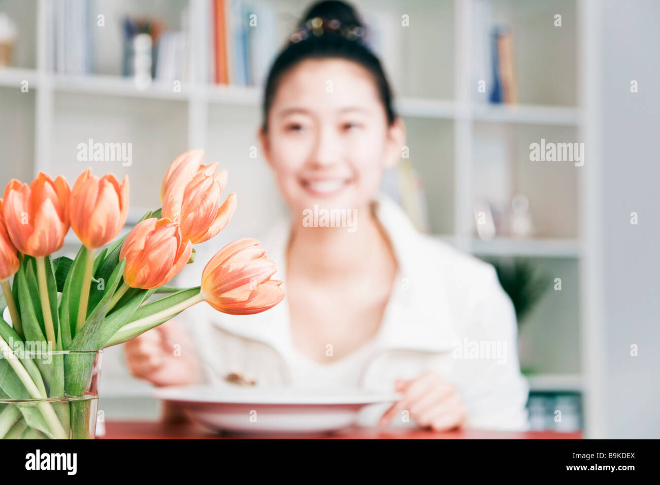 portrait of young japanese girl eating at table focus on tulips in vase ...