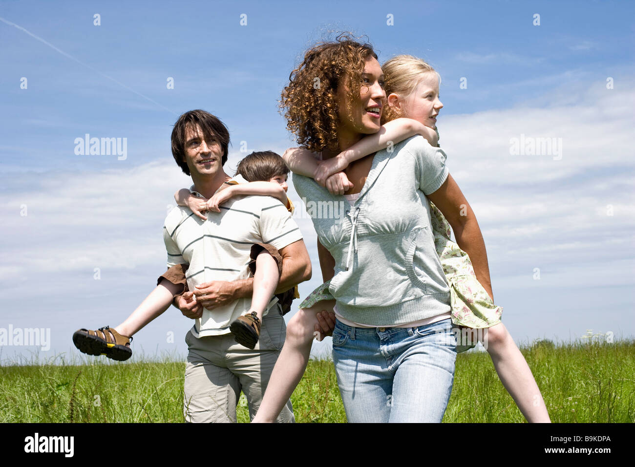 young parents giving their children piggyback ride Stock Photo - Alamy