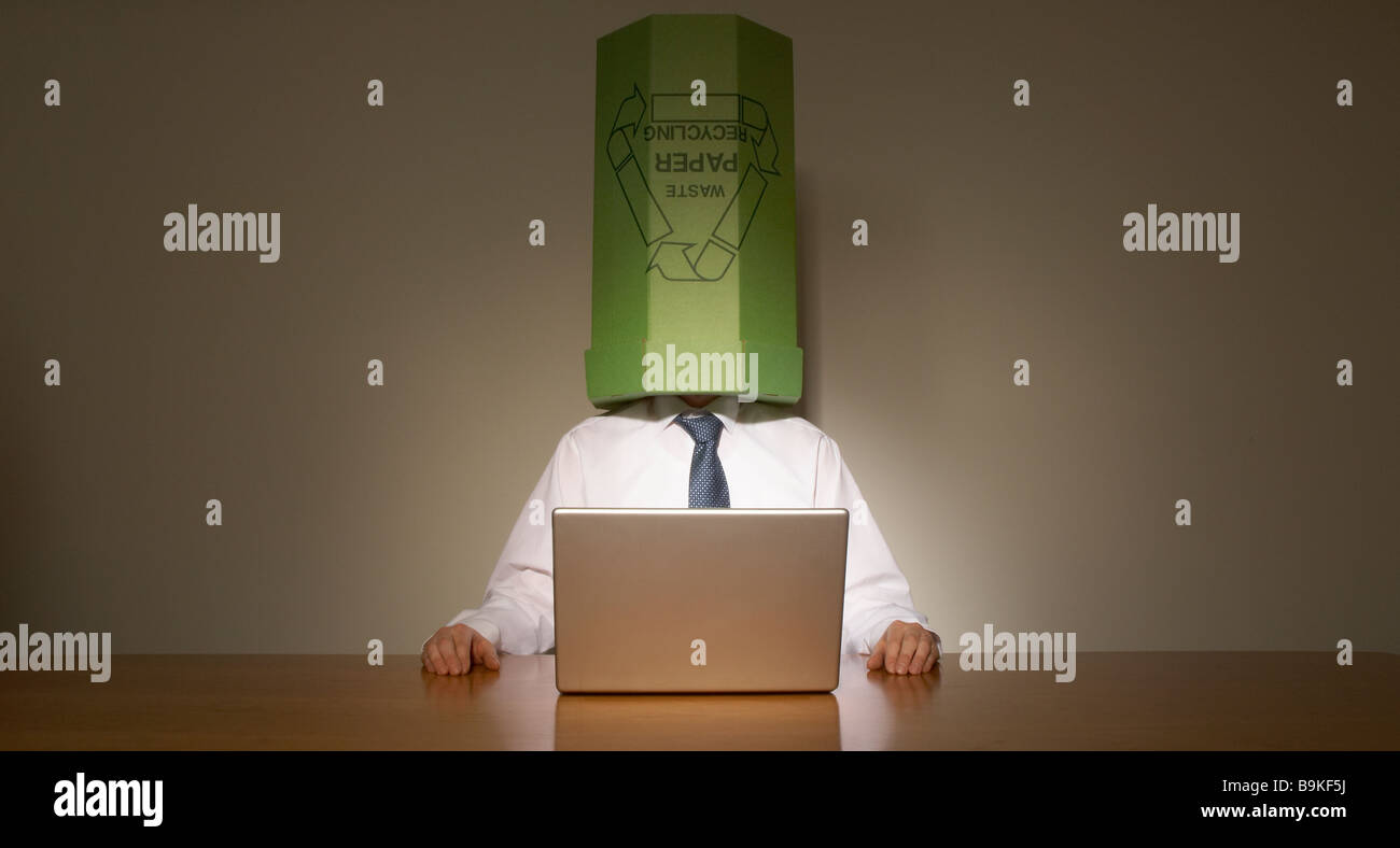 businessman sitting behind computer with wastebasket over his head ...