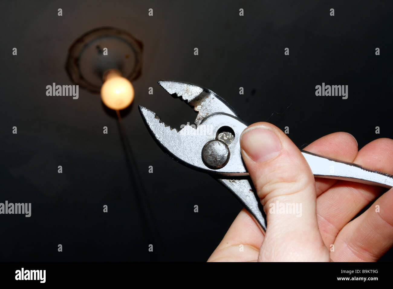 Male hand holding silver ordinary pliers with lightbulb in background ...
