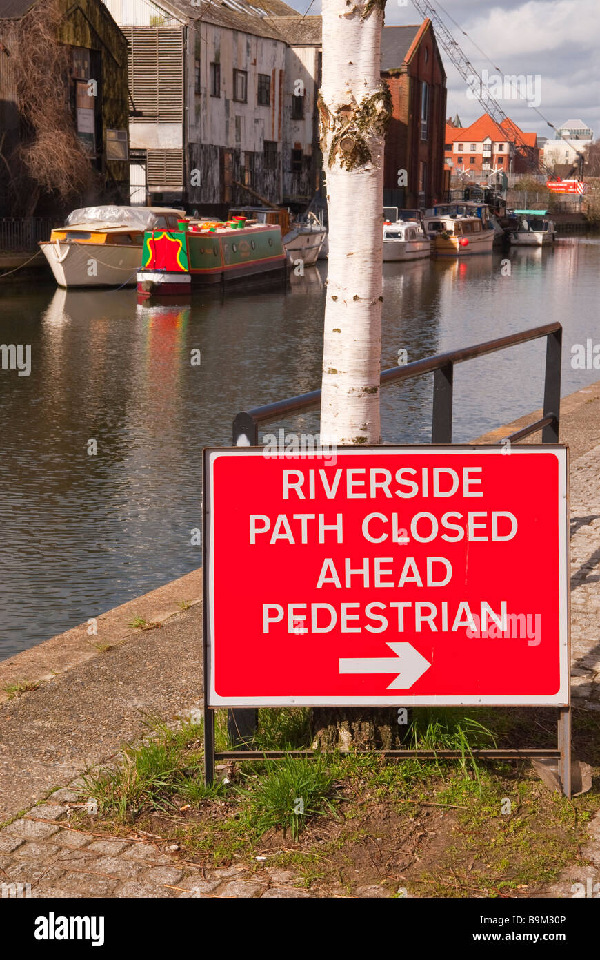 A sign stating the riverside path is closed ahead,pedestrians this way ...