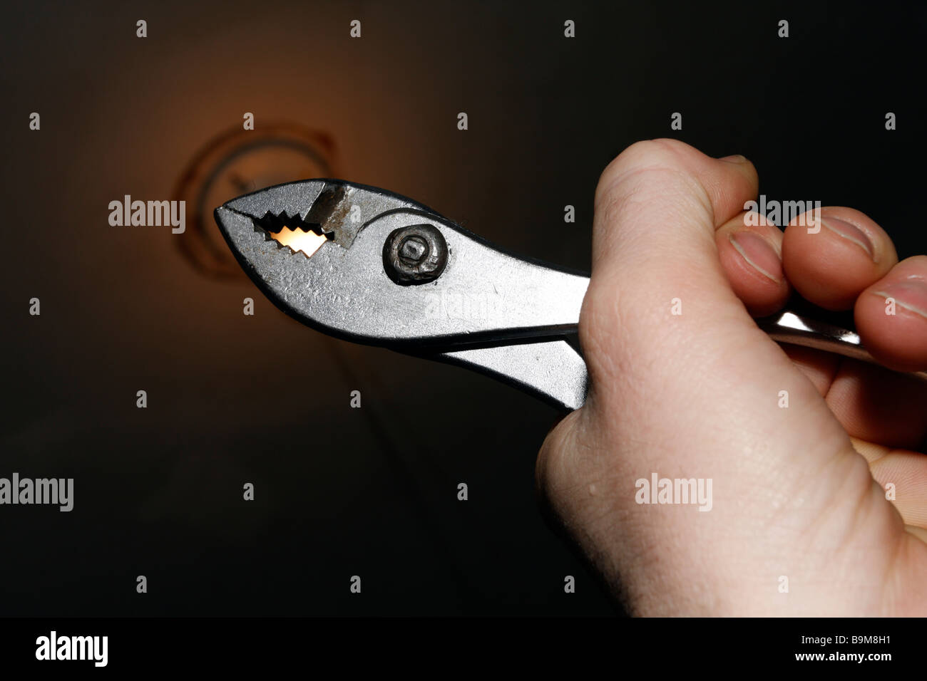 Male hand holding silver ordinary pliers with lightbulb in background ...