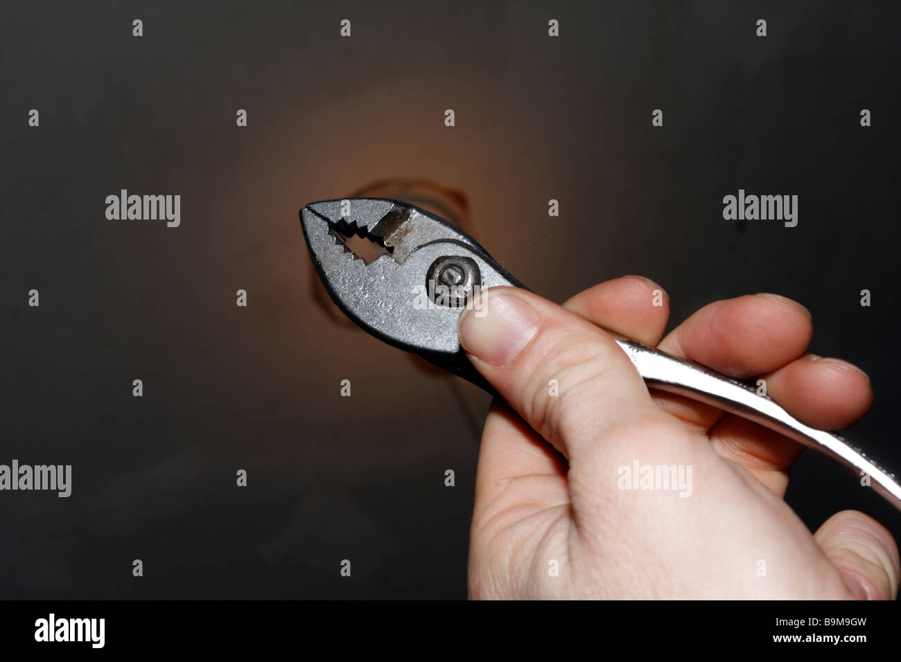 Male hand holding silver ordinary pliers with lightbulb in background ...
