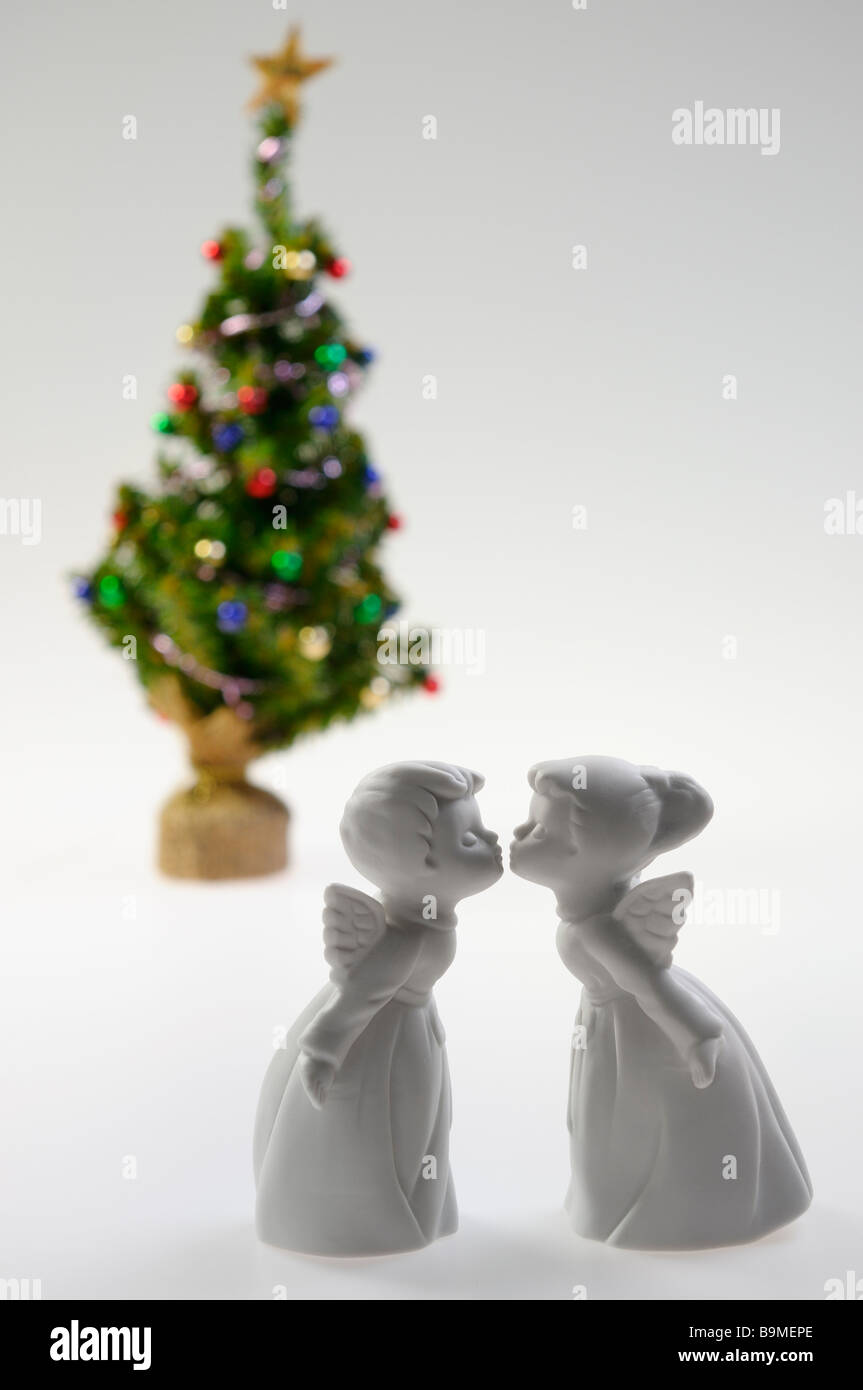 White porcelain boy and girl angels kissing in front of a decorated Christmas Tree on white ...