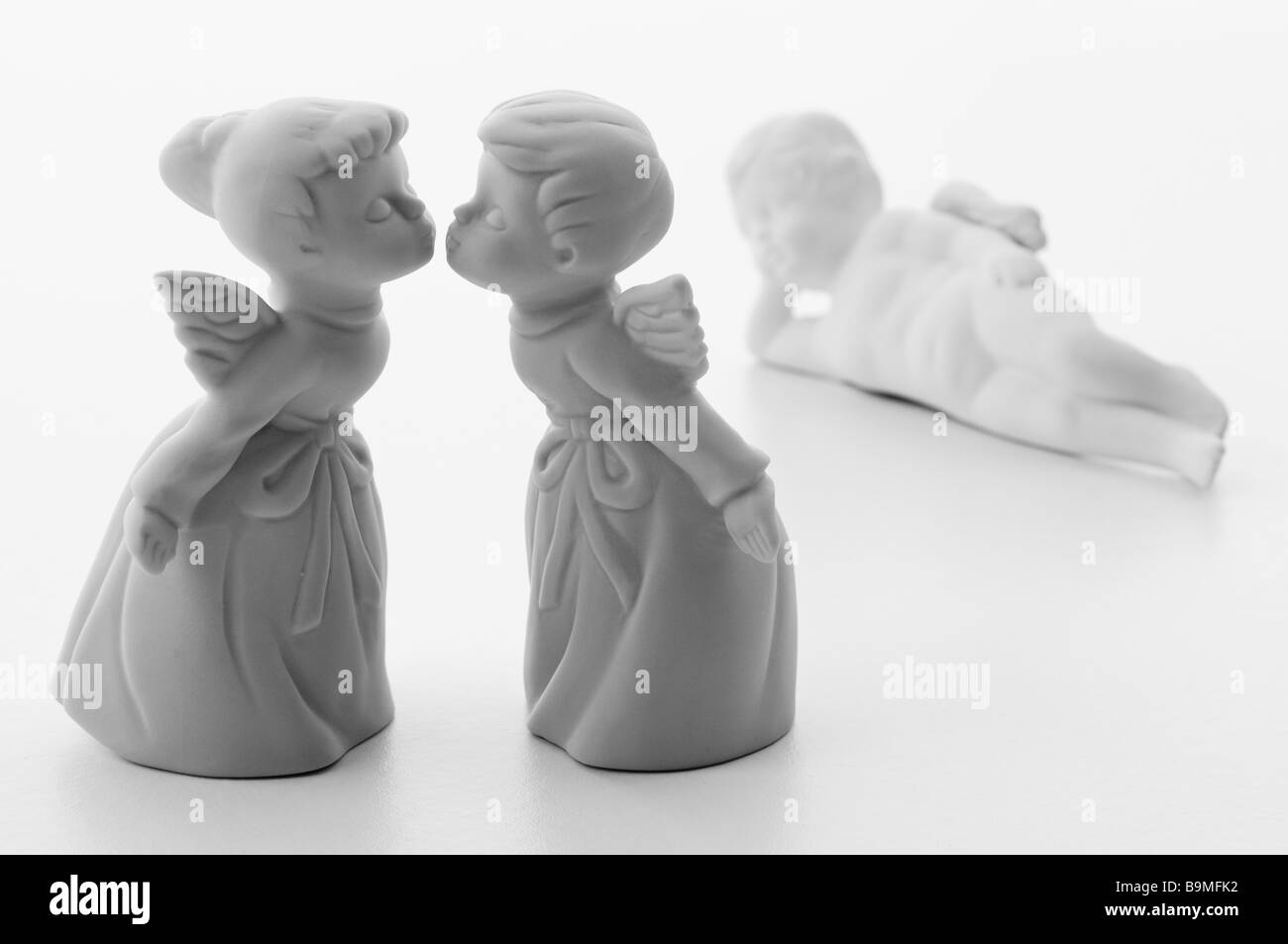 White porcelain boy and girl angels kissing with a third angel lounging in the white background ...