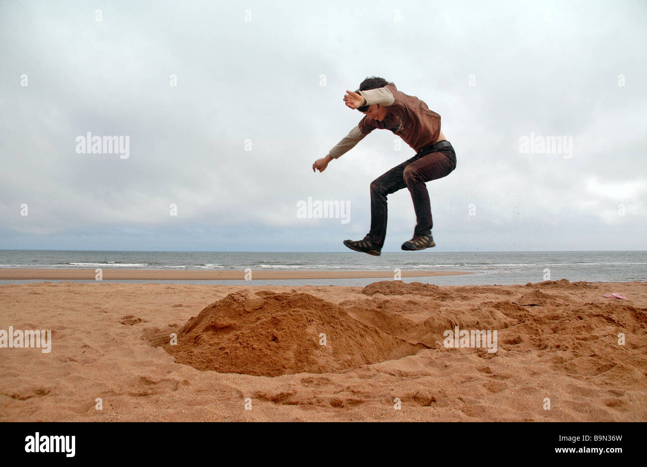 A teenage boy jumps onto a flattened sandcastle Stock Photo - Alamy