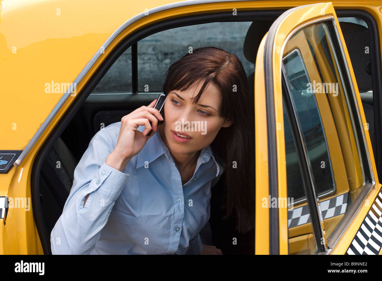portrait of young businesswoman leaving yellow taxi talking on mobile ...