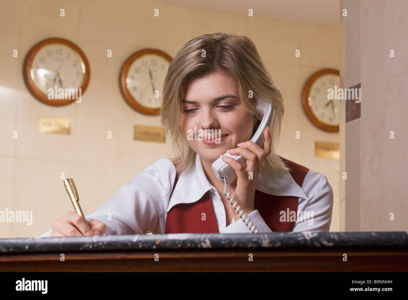 portrait of young hotel receptionist talking on telephone and taking ...