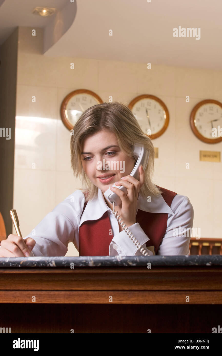 portrait of young hotel receptionist talking on telephone and taking ...