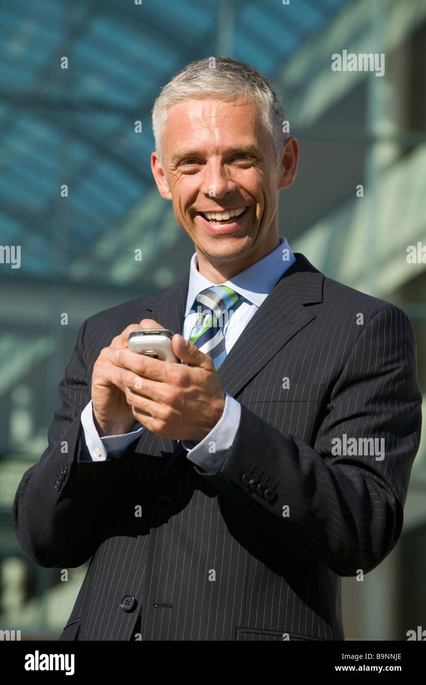 portrait of mature businessman typing text message on mobile phone ...