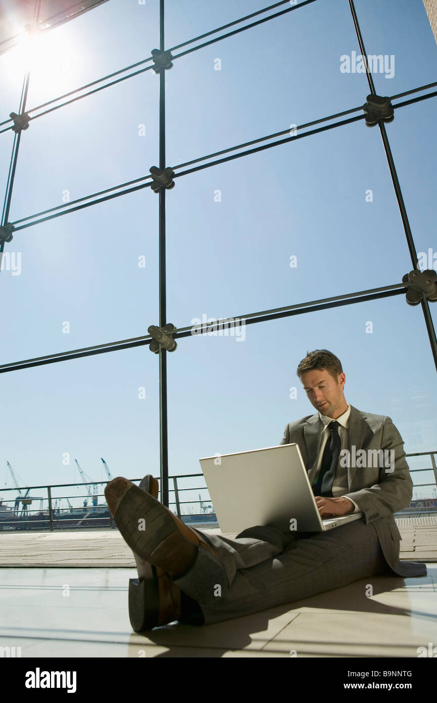 businessman sitting on floor in front of window working with laptop ...