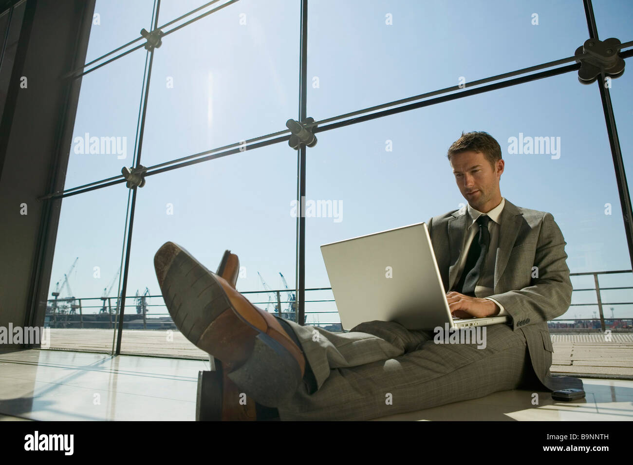businessman sitting on floor in front of window working with laptop ...