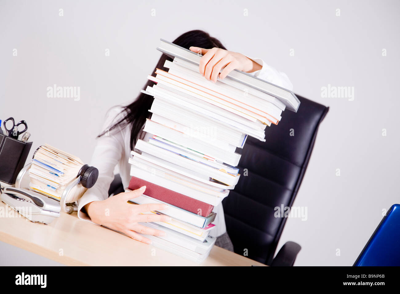 businesswoman sitting on desk hidden behind pile of books Stock Photo ...