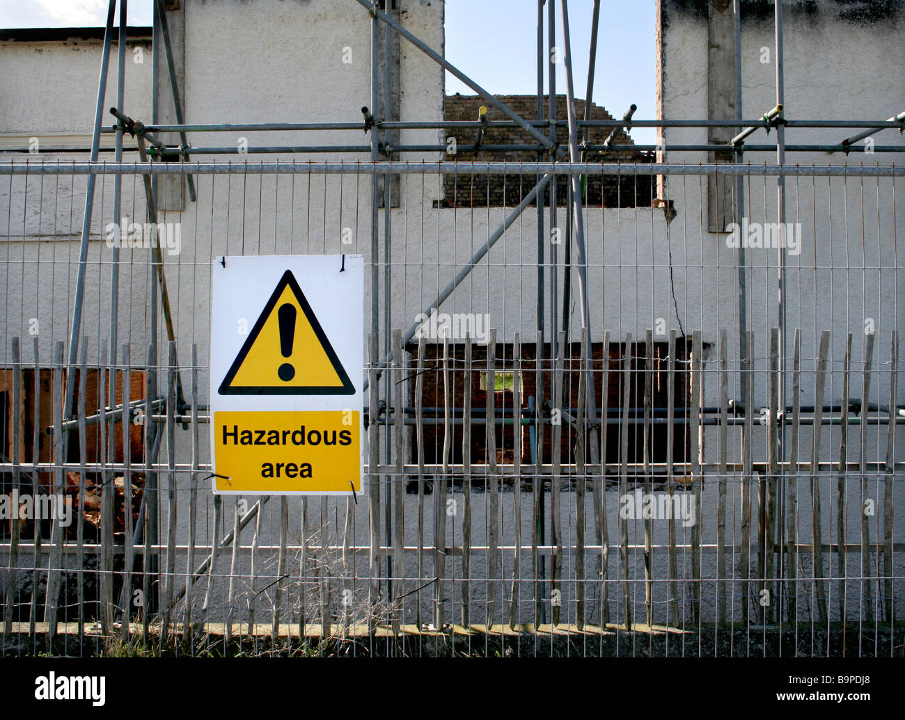 Warning sign attached to fencing outside a burnt out derelict building ...