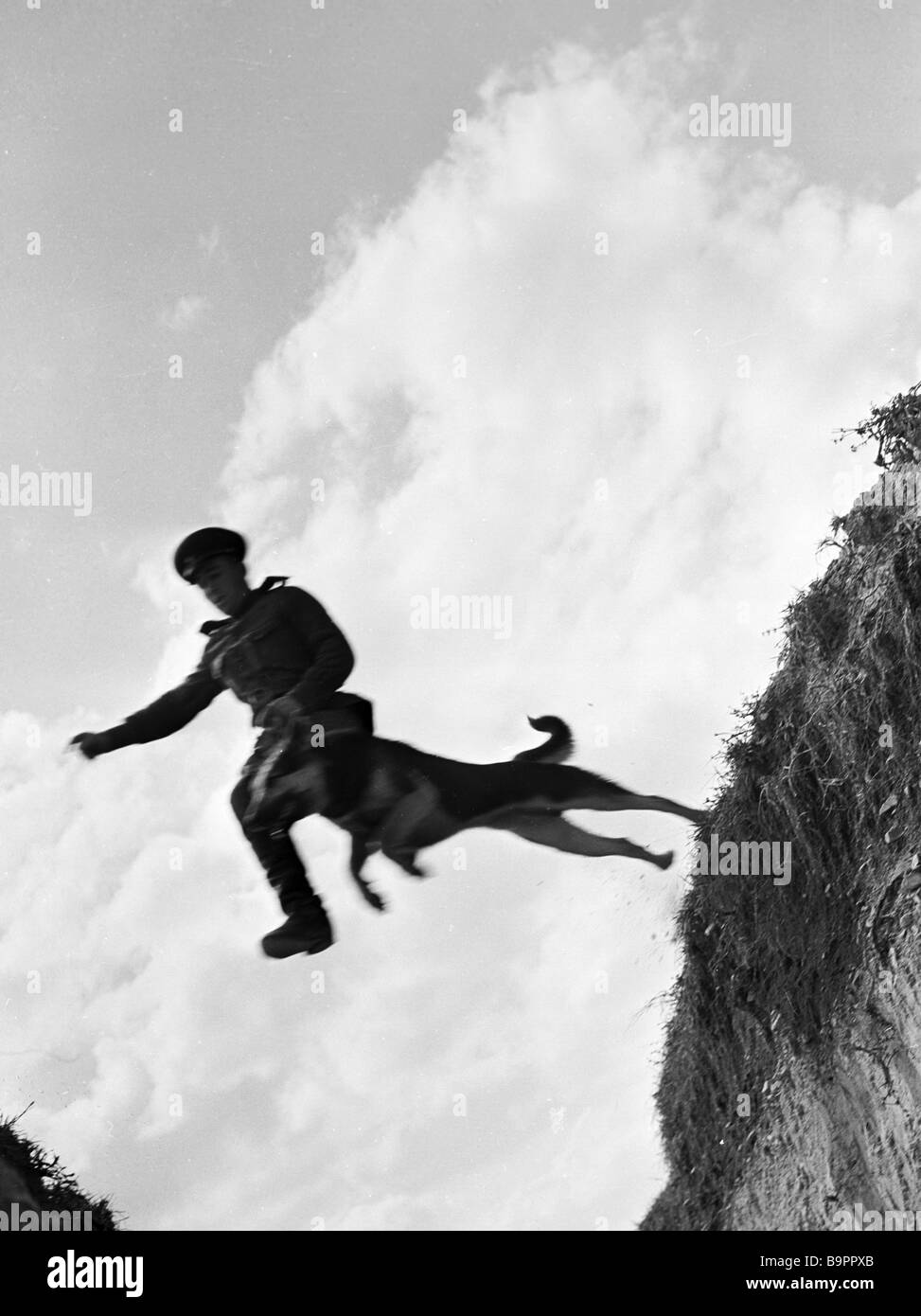 Border guard with dog jumping over a ditch Stock Photo - Alamy