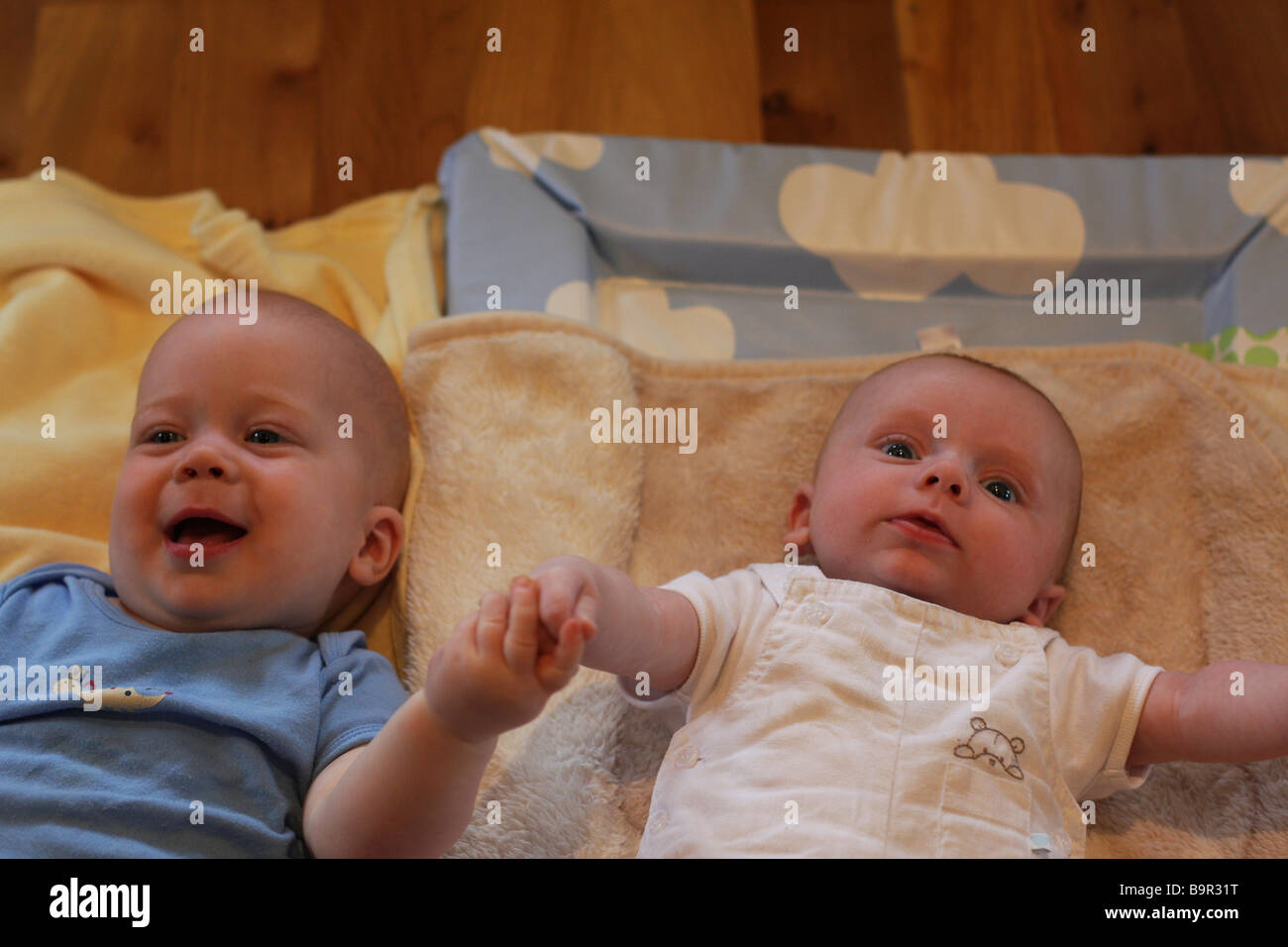 Babies play together holding hands on playmat Stock Photo - Alamy