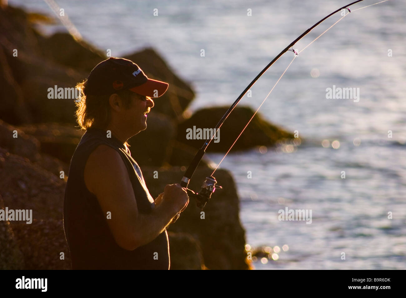 Man fishing off the shore at sunset, Airlie Beach, Queensland ...
