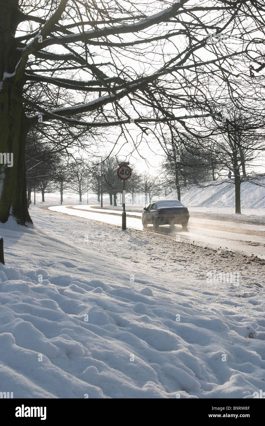 Snow scene with trees and road running through and car in far distance ...