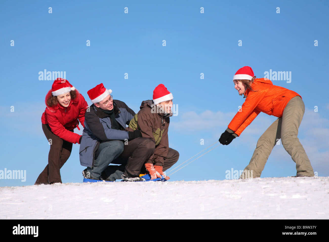 one woman pull two men on sled, other woman push them Stock Photo - Alamy