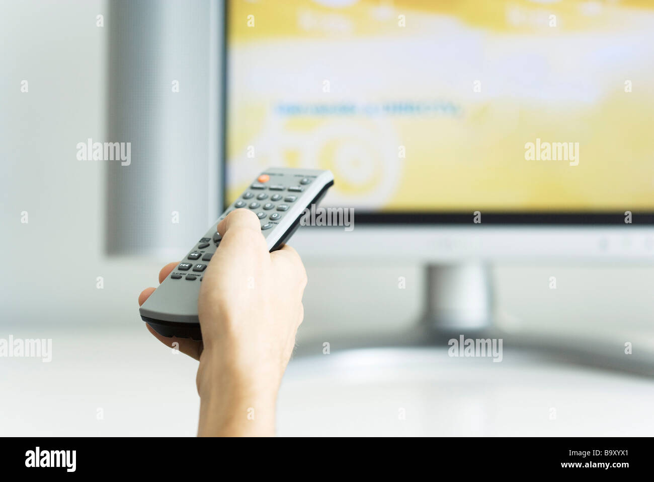 Hand holding remote control, television in background Stock Photo - Alamy