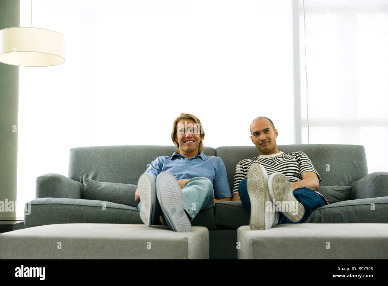 Two men sitting on sofa with feet up, smiling Stock Photo - Alamy
