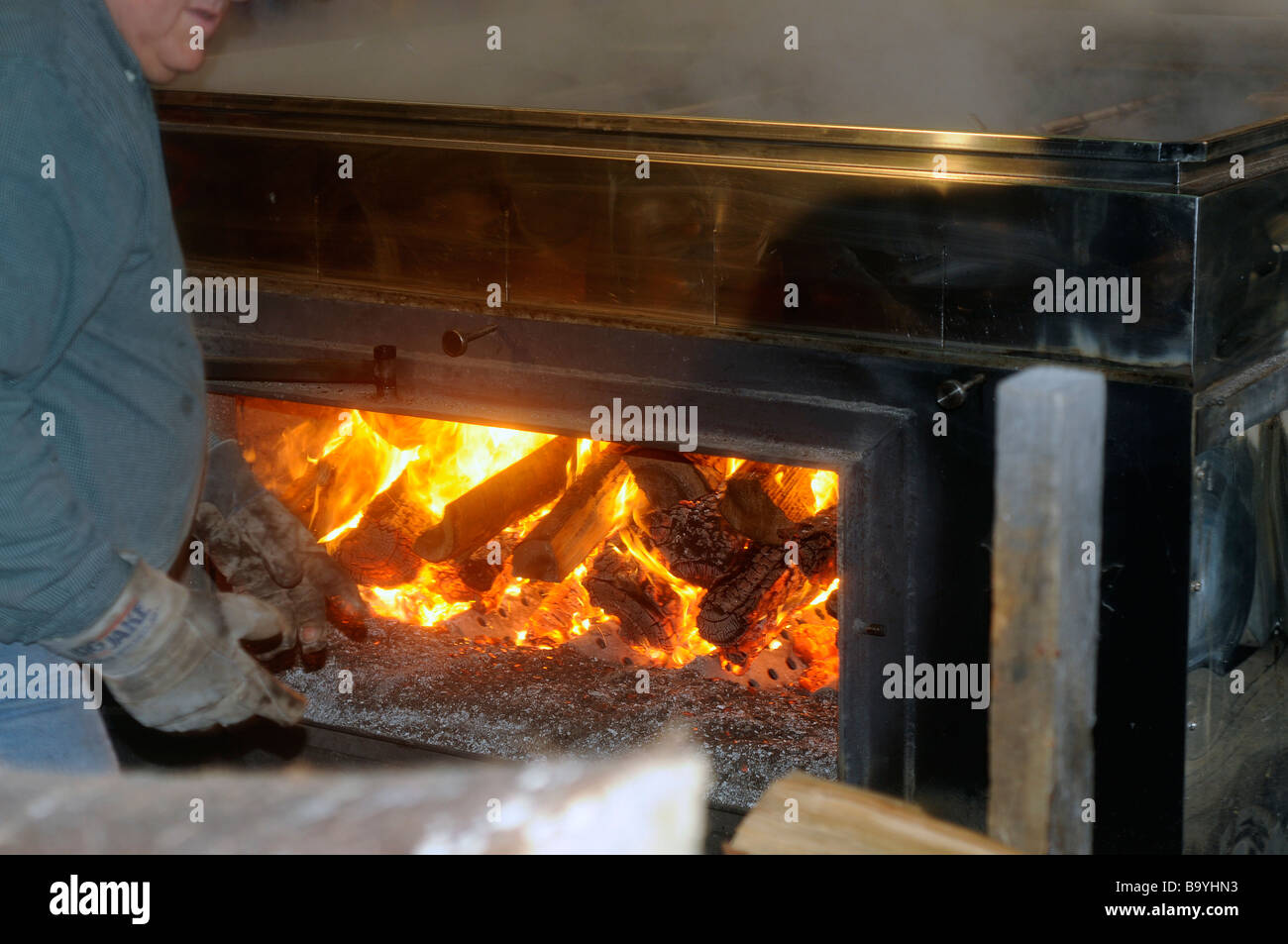 Man feeding fire of boiler making maple syrup Stock Photo - Alamy