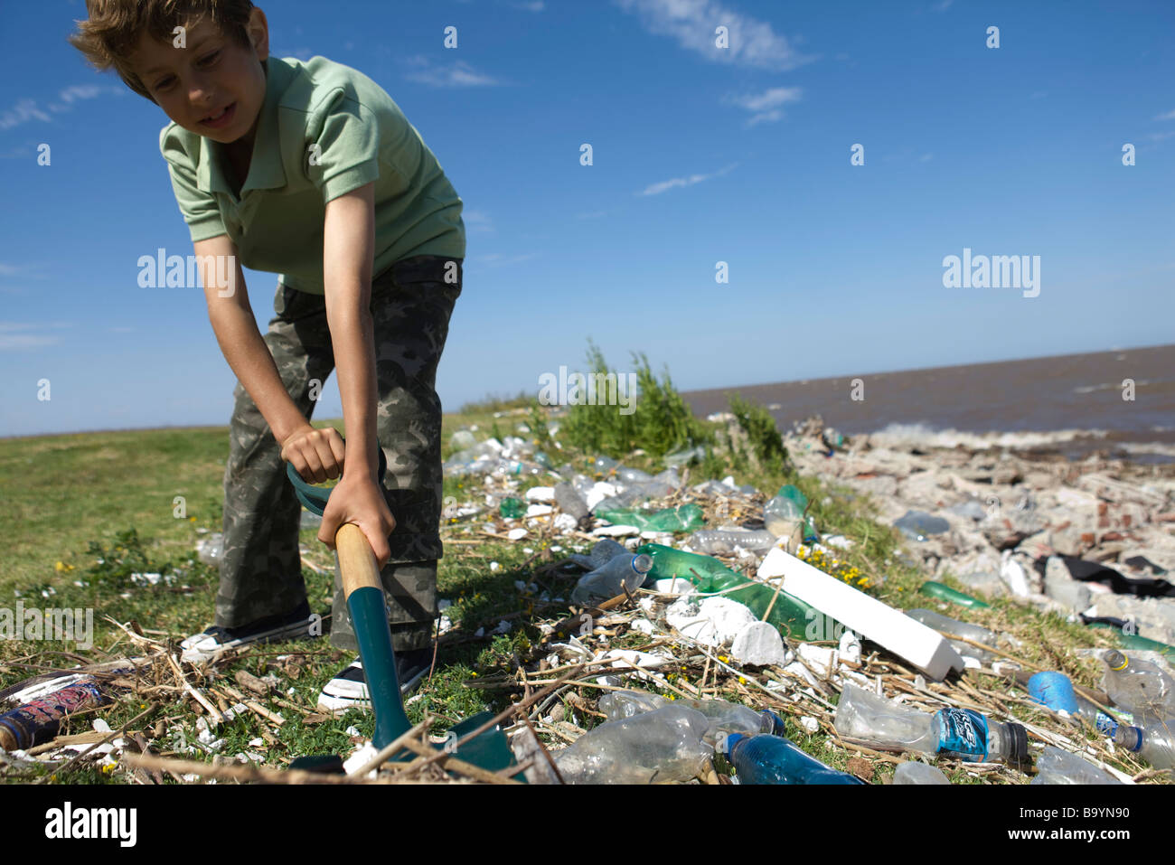 Boy cleaning up polluted shore with shovel, low angle view Stock Photo ...