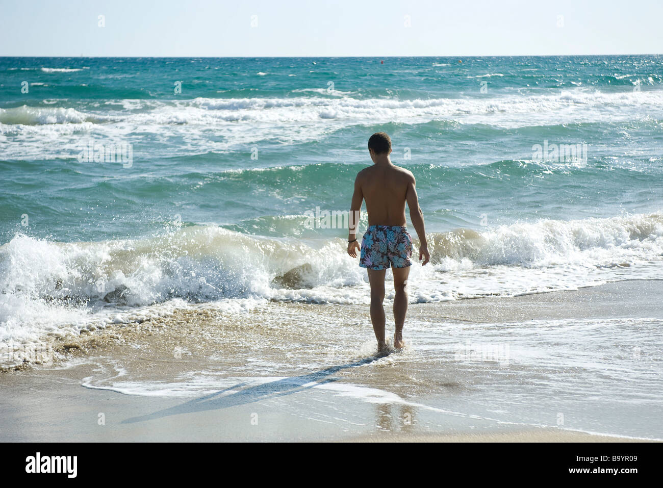 Teen boy walking in surf at beach, rear view Stock Photo - Alamy