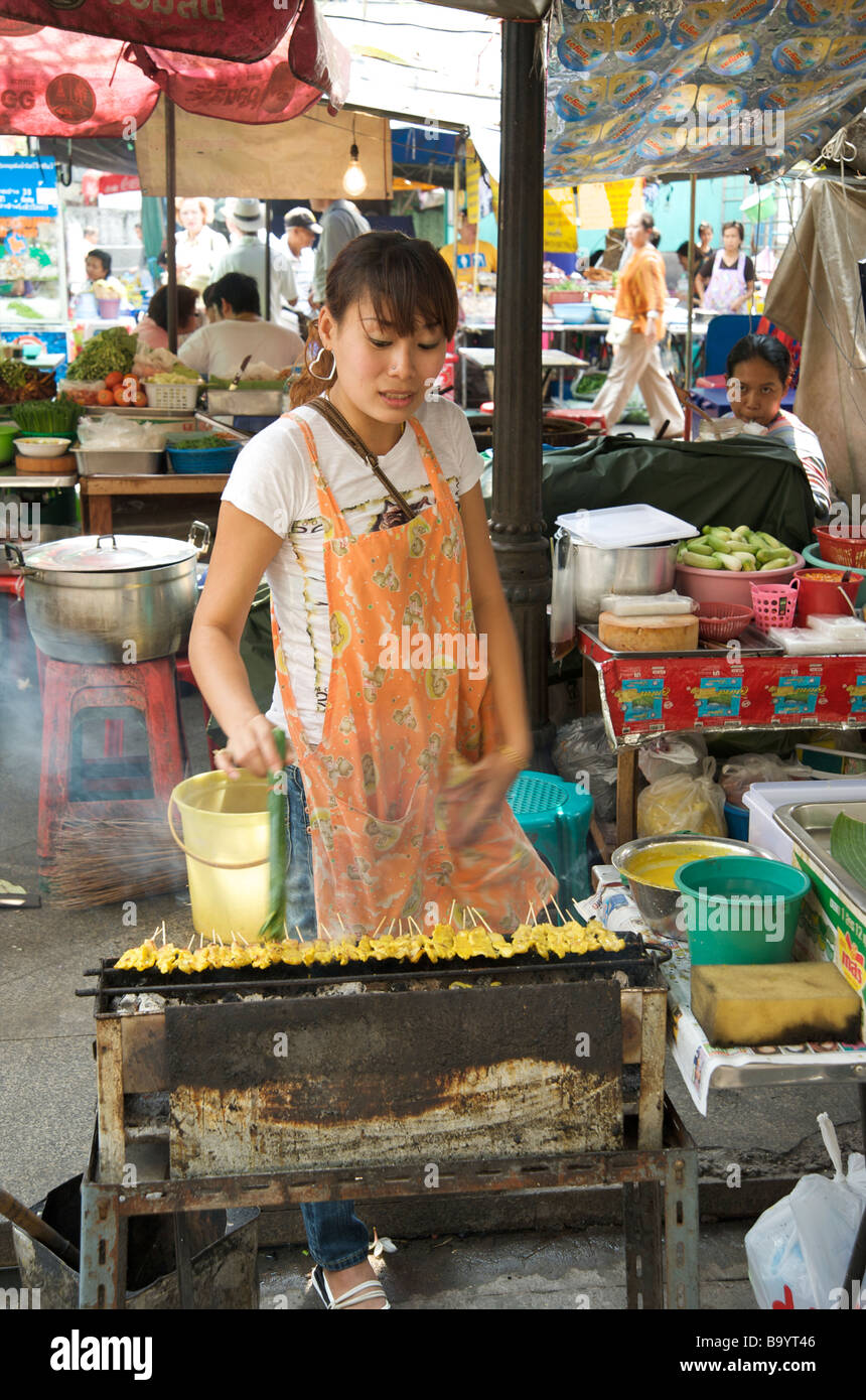 A thai woman grilling chicken satay sticks on her street stall in a ...
