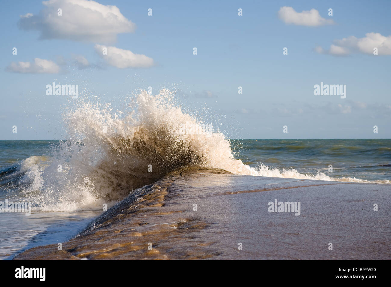 A large wave explodes in streams of water over a stone jetty with a ...