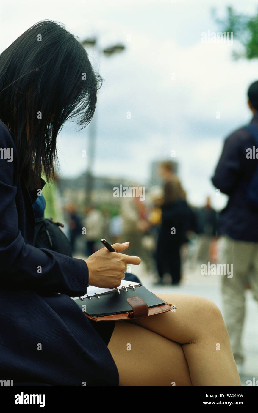 Businesswoman sitting outside, legs crossed, writing in agenda Stock ...
