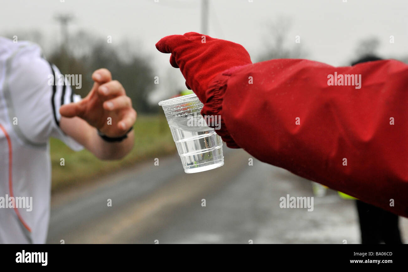 gloved hand passing container of drinking water to passing runner in ...
