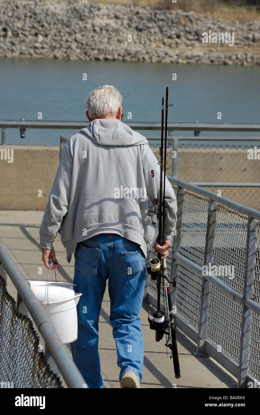 An older man walking down the fishing pier getting ready to go fishing ...