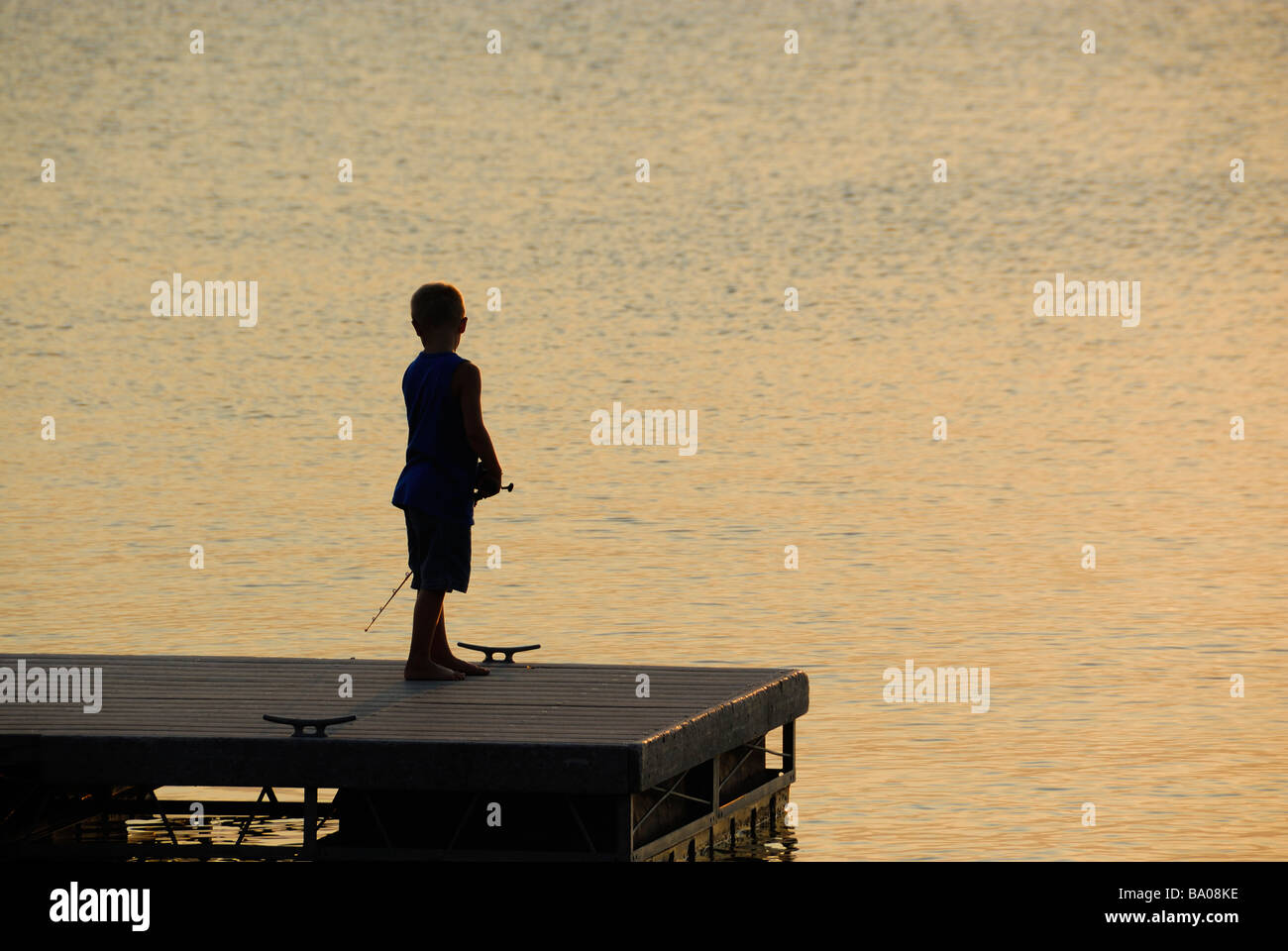 A young boy standing on a fishing pier waiting on the fish to bite ...