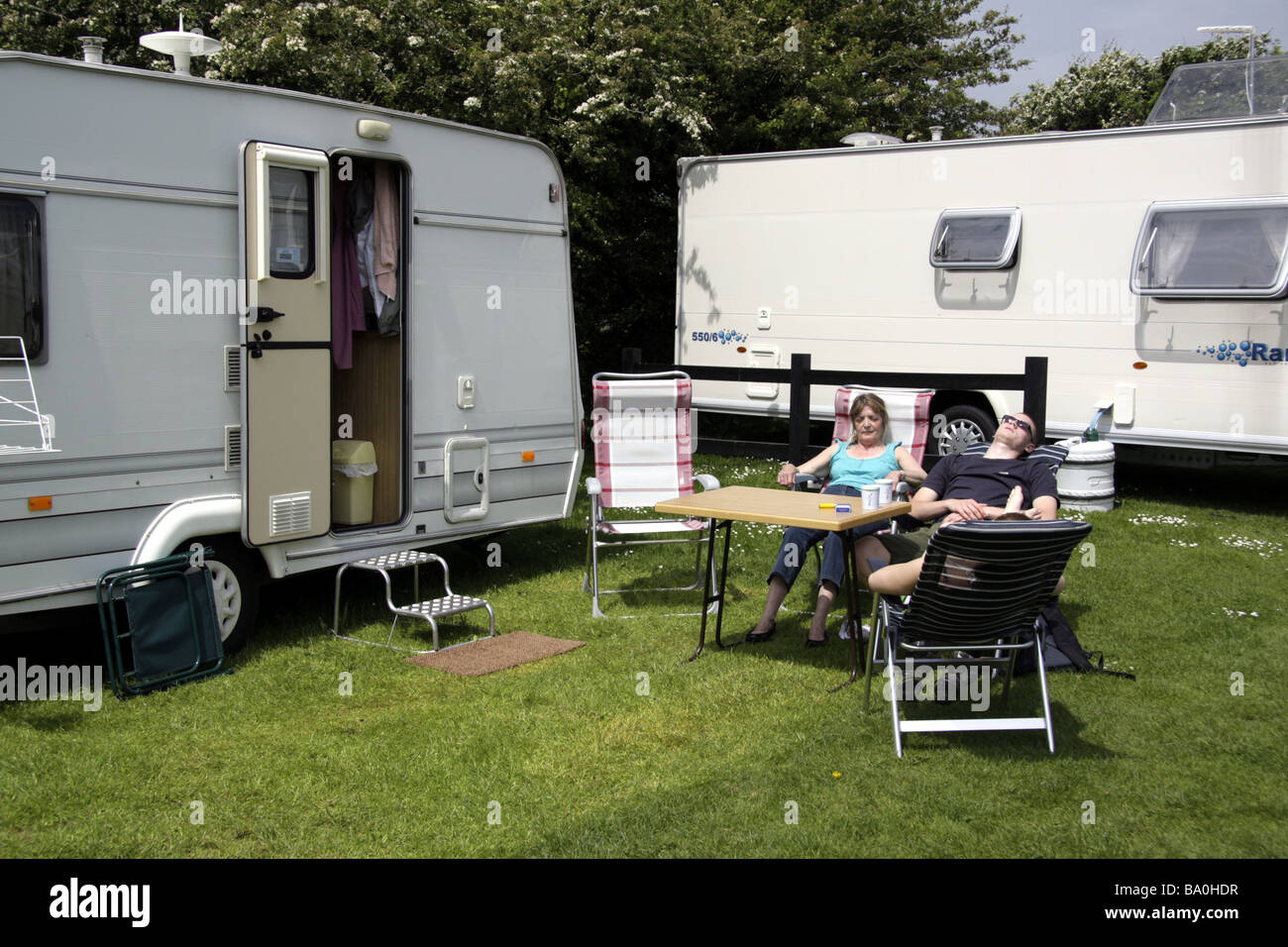 Three people relaxing in the sunshine outside a touring caravan while ...