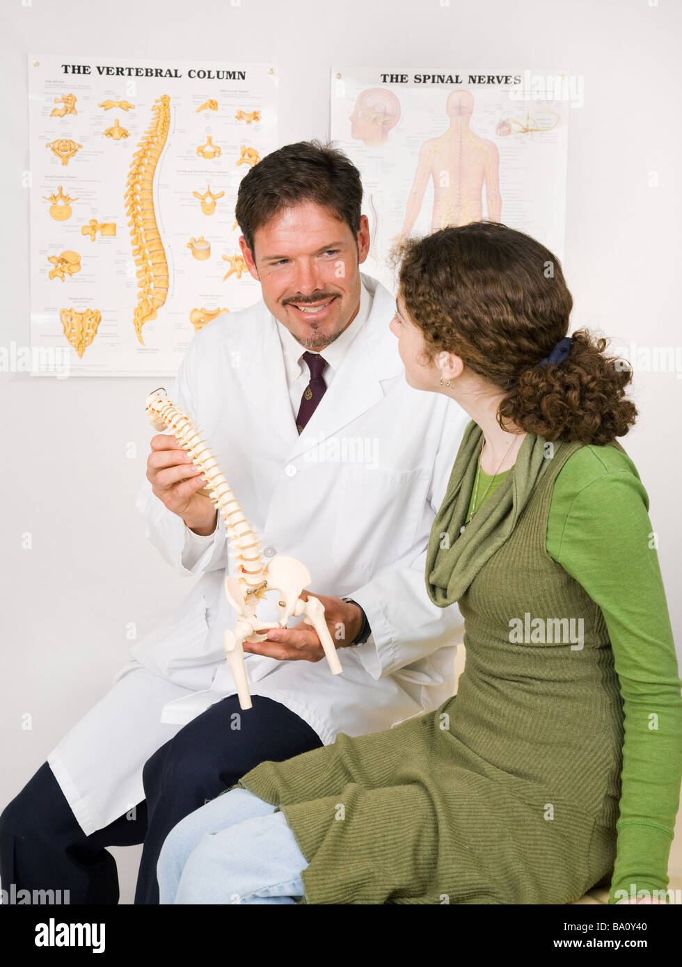Friendly smiling chiropractor uses a model to explain the spinal ...