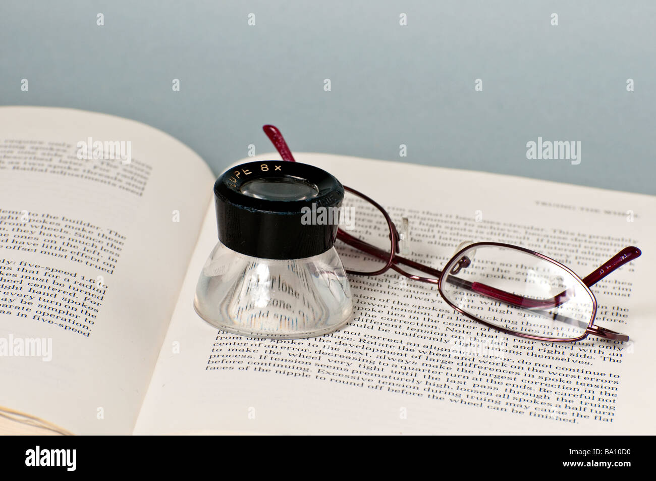 Open book with reading glasses and a magnifying lupe Stock Photo - Alamy