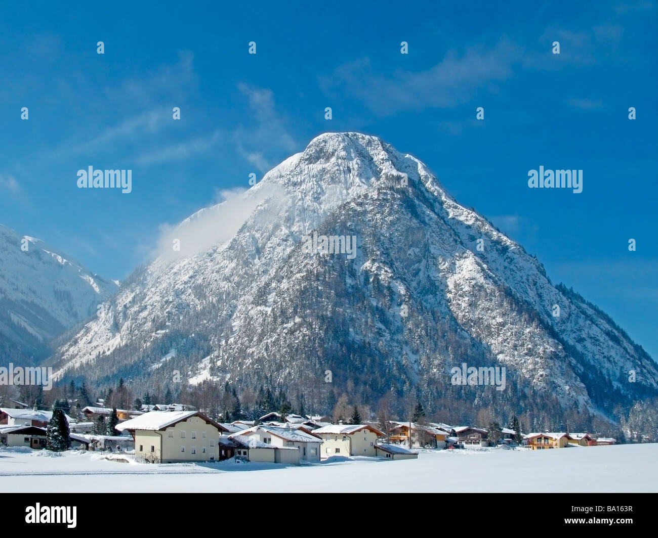 Pretty village at the footage of Tirol mountains in blue ski winter day ...