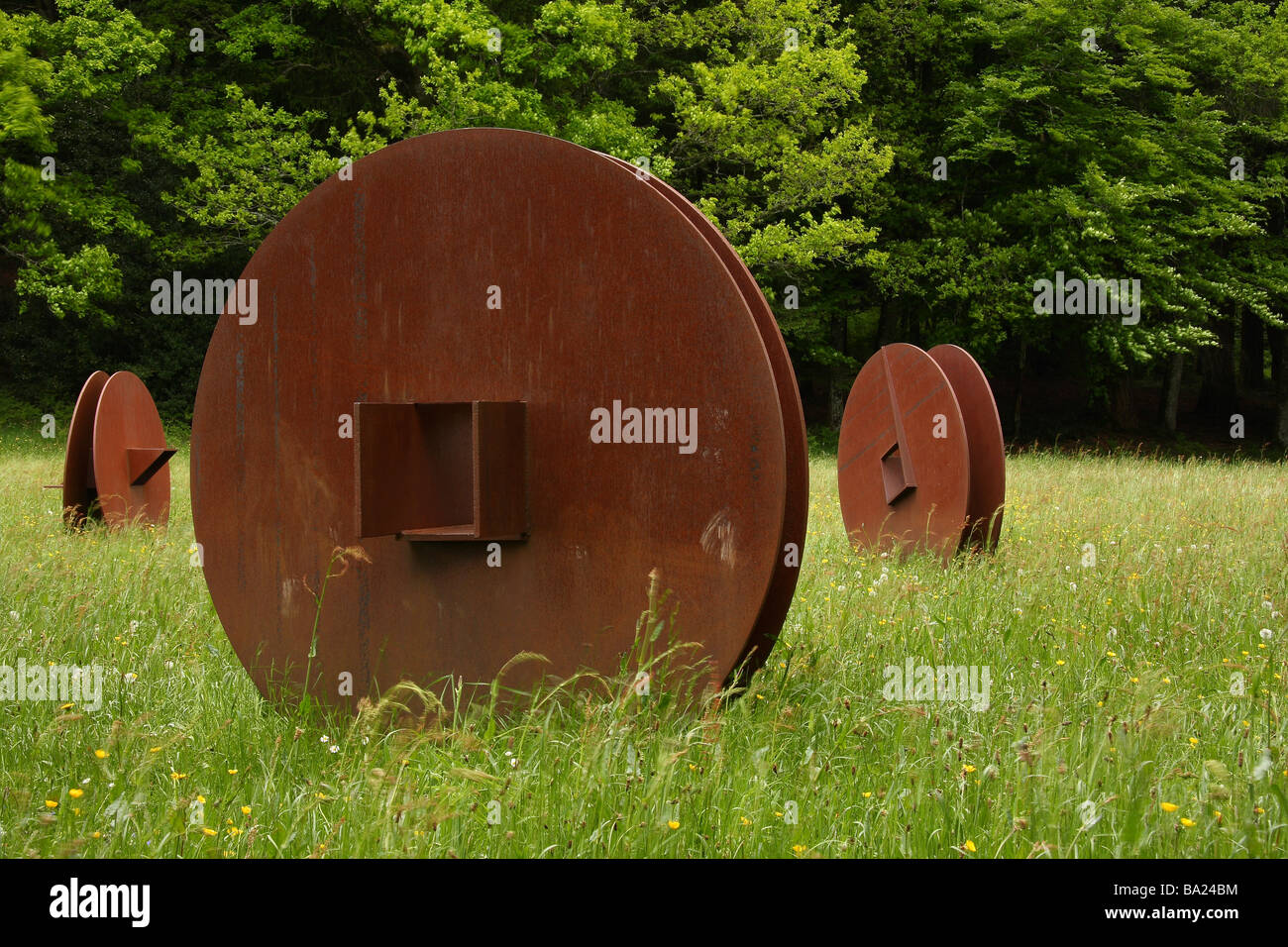 A sculpture of three large rusty metal reels in a field Stock Photo - Alamy