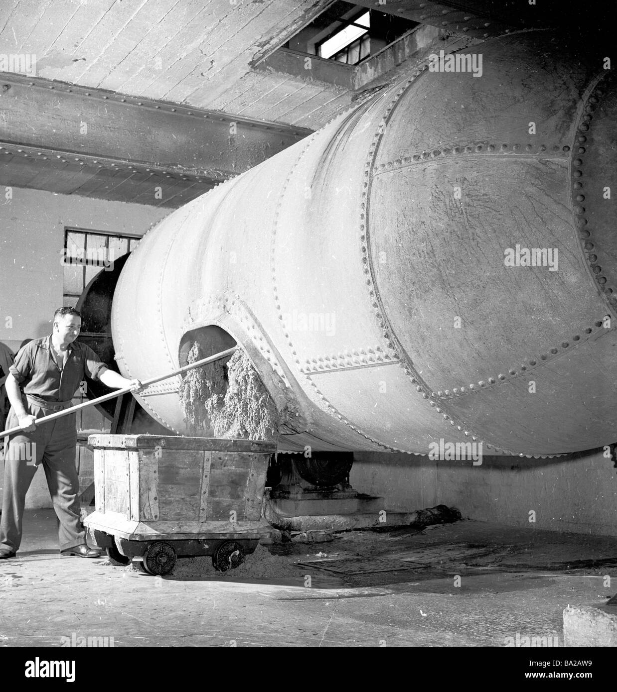 1950s, inside a a papermaking factory, a male worker with a long pole ...