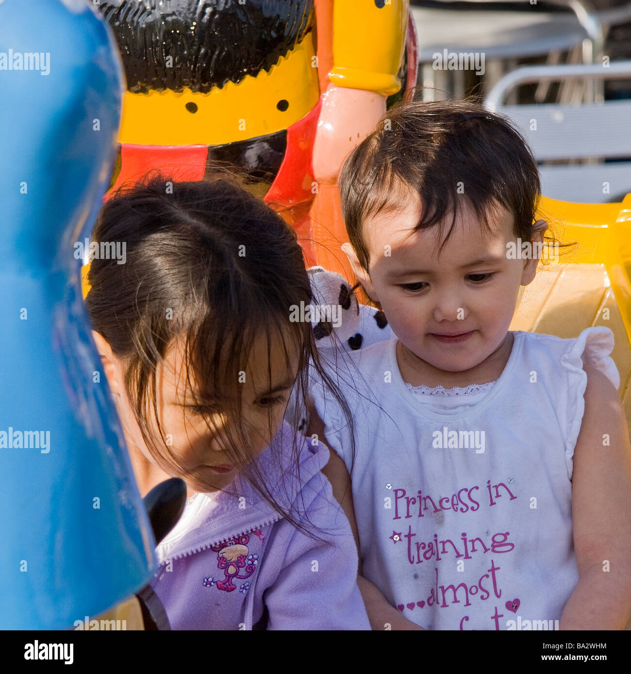 Two half-Thai sisters play on an outside arcade ride in the summer at ...