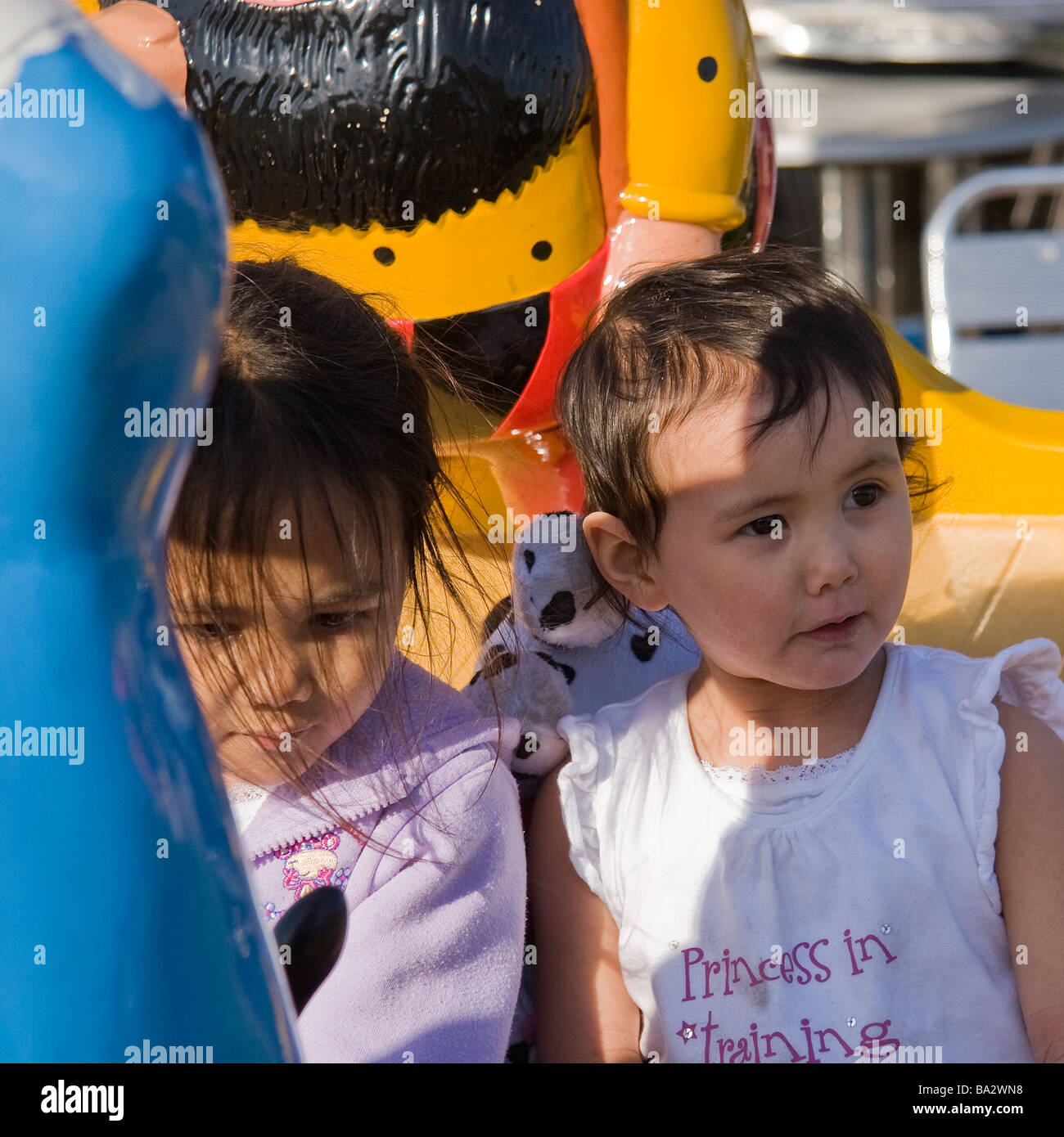 Two half-Thai sisters play on an outside arcade ride in the summer at ...
