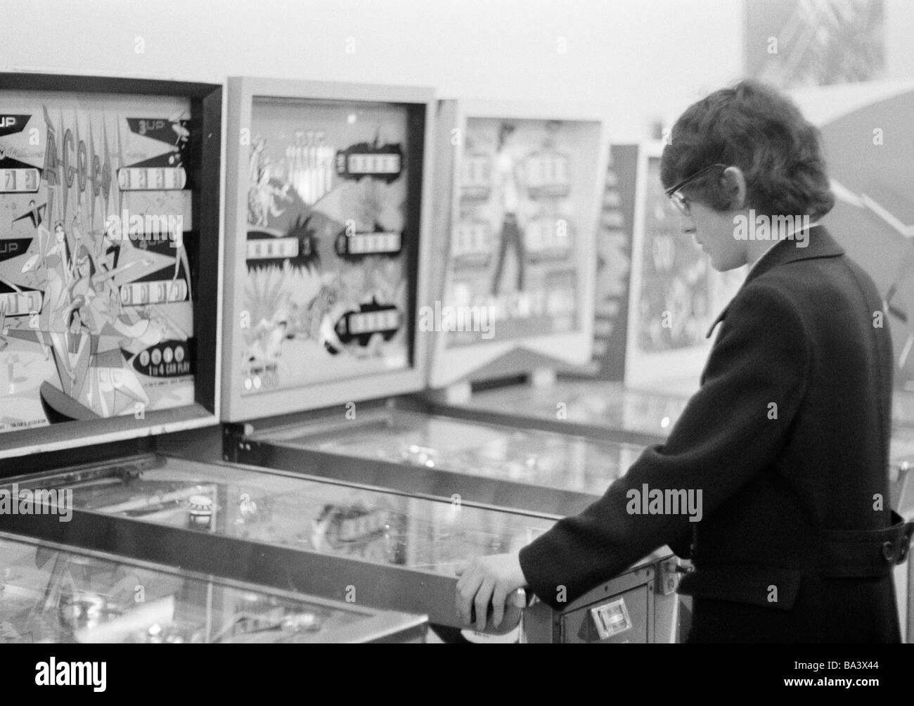 Seventies, black and white photo, people, young boy plays at a pinball ...