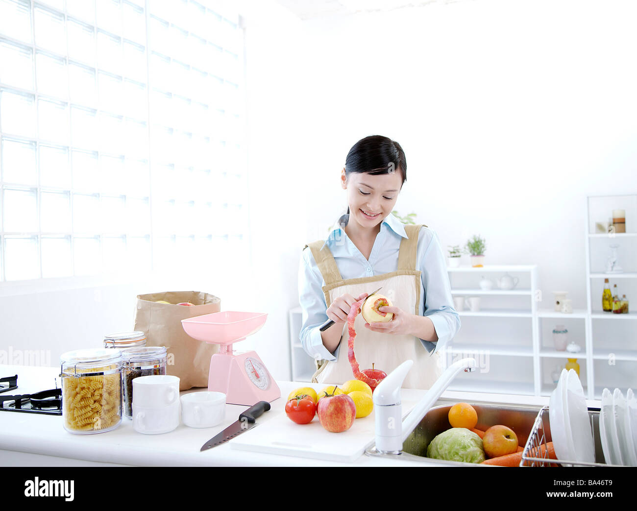 Young woman peeling apple smiling in kitchen Stock Photo - Alamy