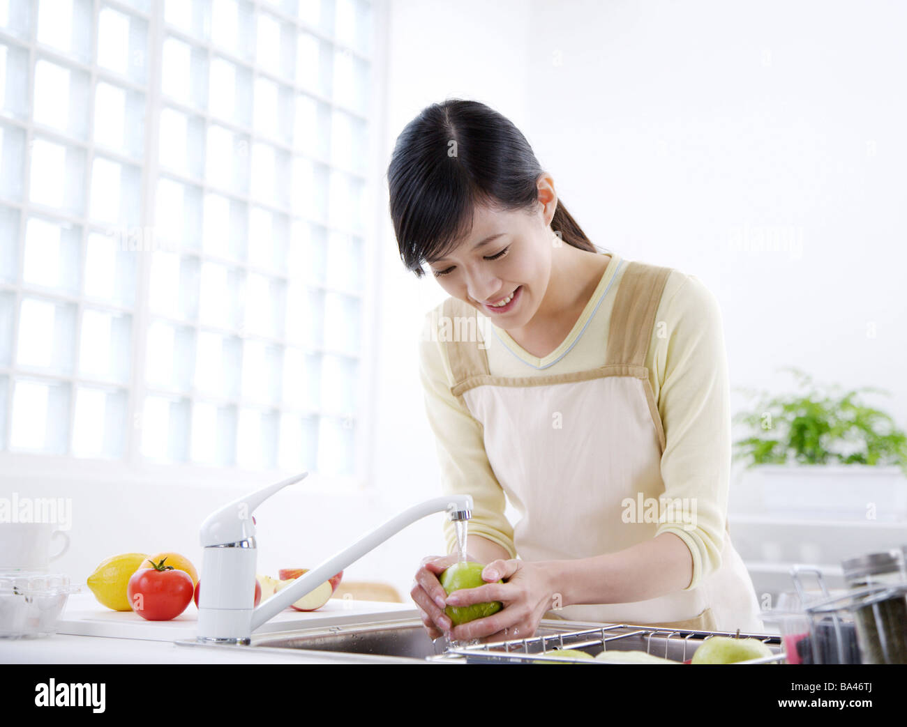 Young woman washing apple under tap smiling Stock Photo - Alamy