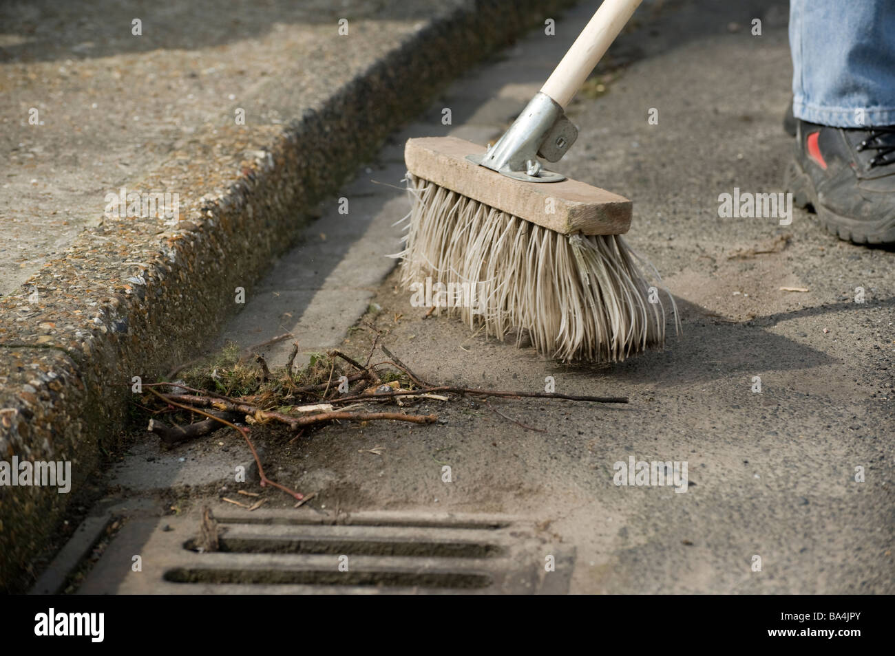 Using a broom to sweep debris off the road in a street in England Stock ...
