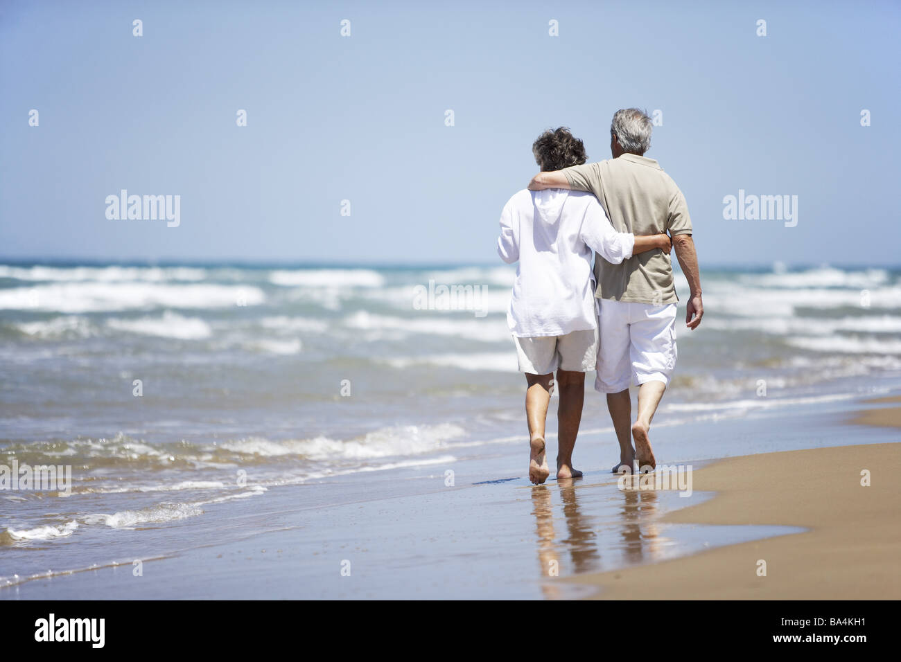 Sandy beach senior-pair arm in arm walk back-opinion series people ...