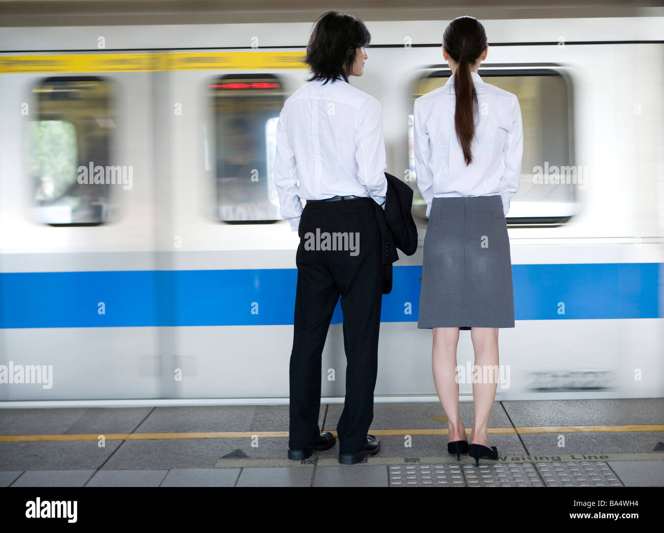 Businessman and businesswoman standing on train platform rear view ...